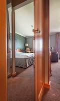 Quarto de hotel com uma cama, uma cadeira, uma luminária e vista para o corredor.