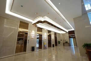 Um hall de hotel moderno com piso reluzente, luminária central e balcão de recepção.
