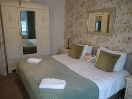 Quarto com uma cama grande, guarda-roupa, mesa de cabeceira e espelho na parede.