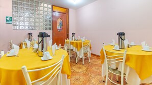 Uma área de refeições com mesas amarelas e cadeiras brancas, equipada com cafeteiras e guardanapos brancos.
