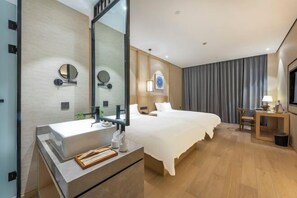 Quarto de hotel moderno com uma cama grande, uma toucador com espelho, uma escrivaninha e uma janela ampla com cortinas.