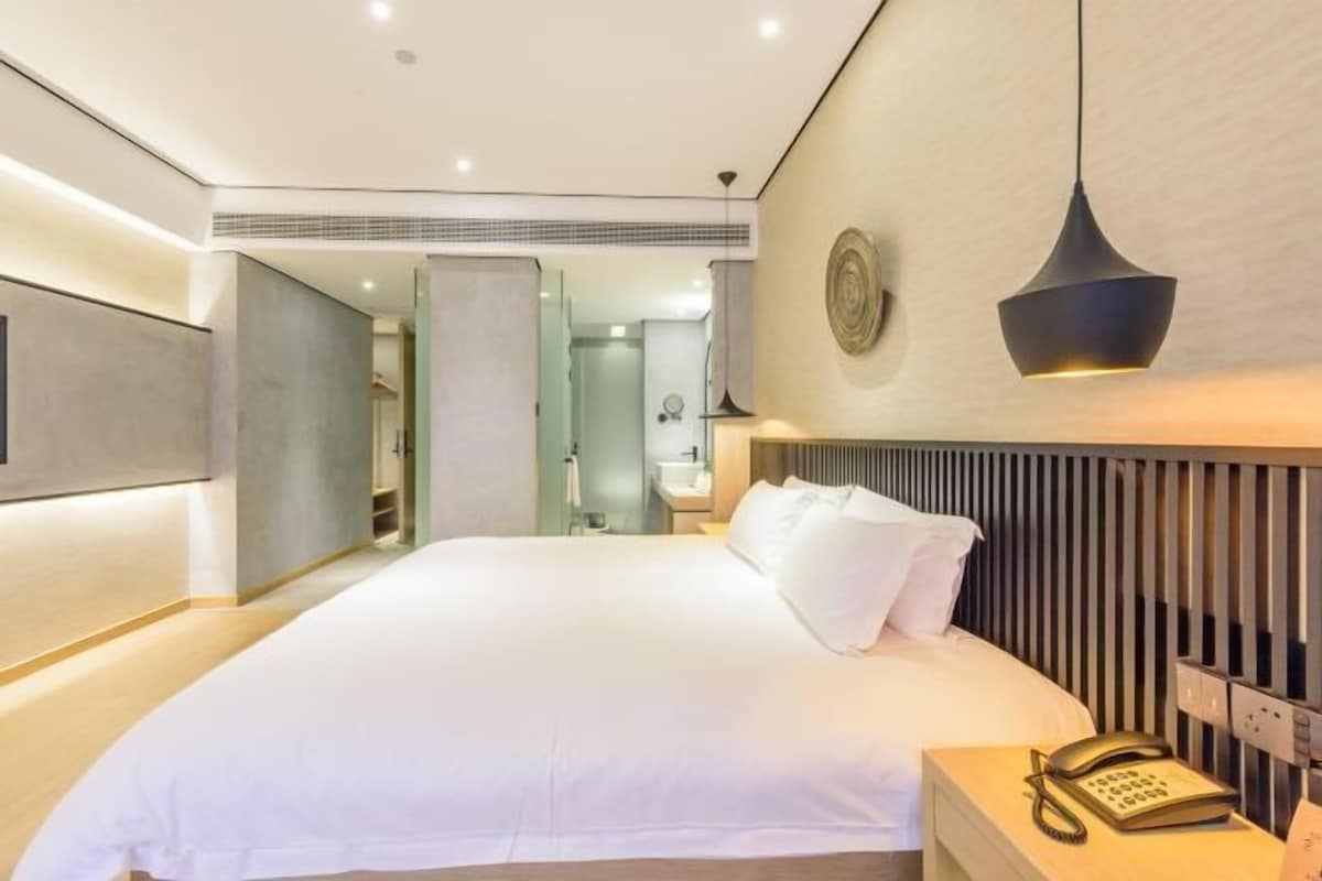 Quarto de hotel moderno com uma cama grande, telefone ao lado da cama e luminária fixada na parede.