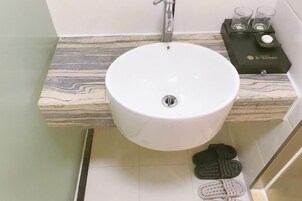 Casa de banho com bancada de mármore, lavatório branco e um par de chinelos.