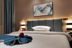 Quarto de hotel com uma cama grande, cabeceira, pintura abstrata na parede e abajures laterais.
