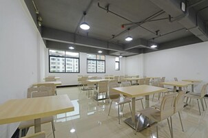 Sala de conferência com várias mesas e cadeiras, grandes janelas e teto alto com tubulações aparentes.