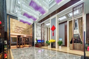 Um saguão de hotel com piso de mármore, balcão de recepção e um grande candelabro.