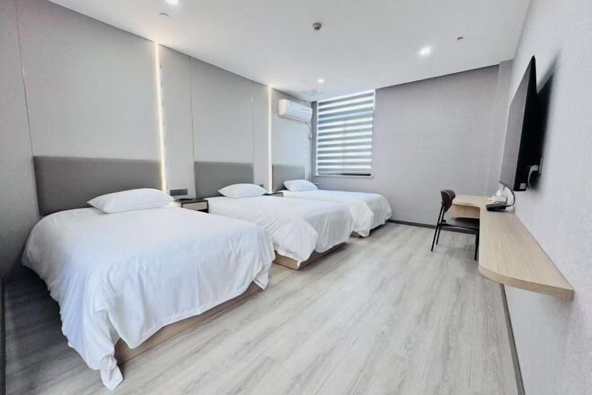 Quarto de hotel moderno com três camas de solteiro, uma escrivaninha e uma televisão de tela plana presa na parede.