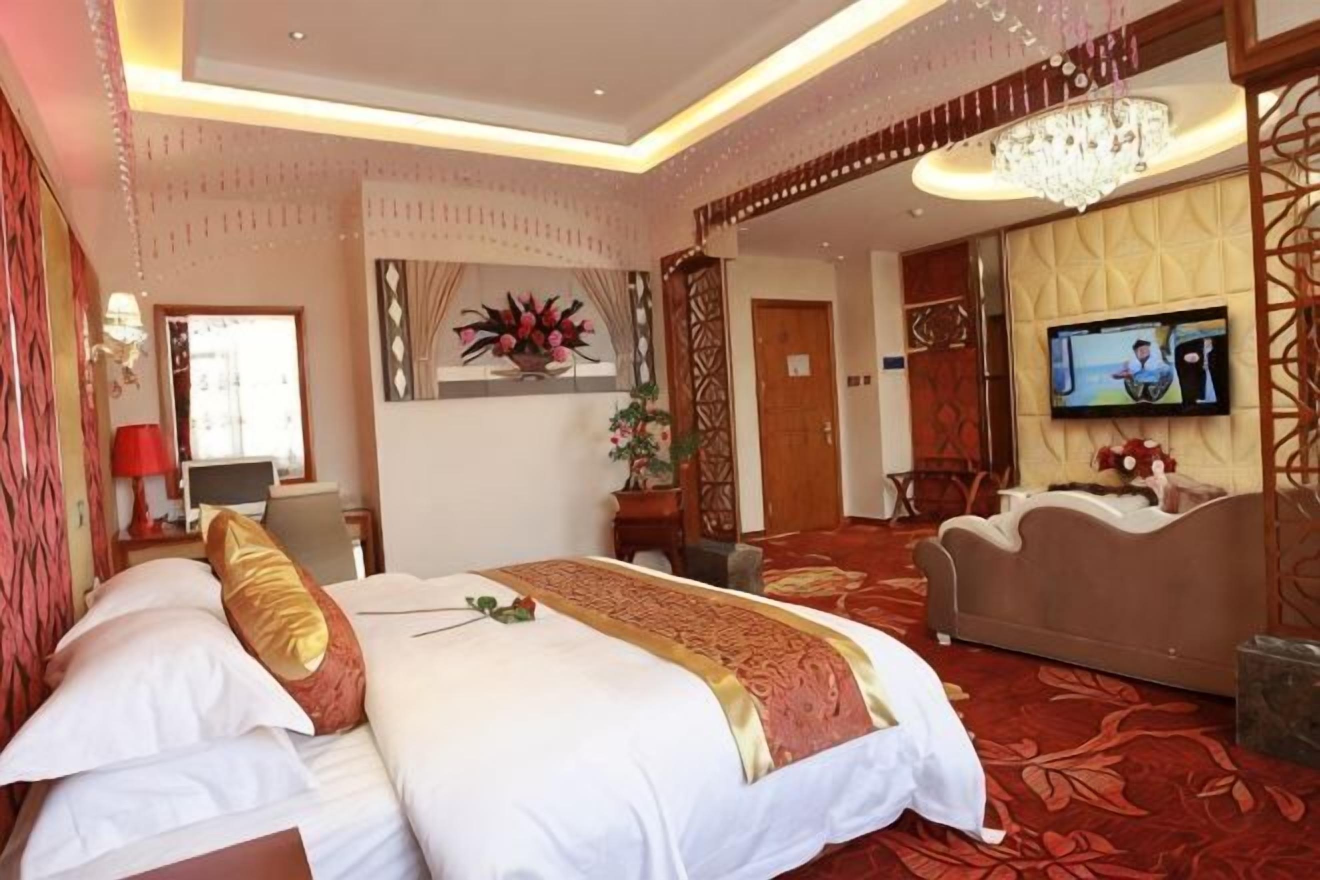 Quarto de hotel com uma cama grande, televisão, sofá e um detalhe decorativo na parede.