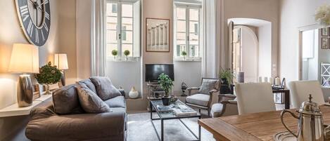 Uma sala de estar com sofá, mesa de centro, televisão e objetos decorativos.