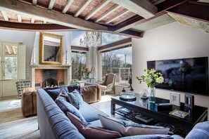 Uma sala de estar com lareira, um sofá grande, uma televisão e um candelabro.