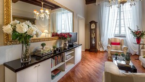 Uma sala de estar com um espelho grande, um candelabro, um relógio e uma televisão.