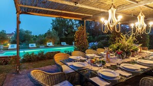 Uma área de refeições ao ar livre com cadeiras e mesas de vime dispostas para uma refeição, com vista para uma piscina.