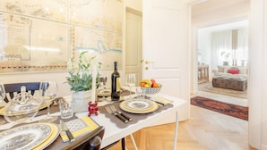Uma sala de jantar com uma mesa branca posta para quatro pessoas, um mapa na parede e vista para a sala de estar.