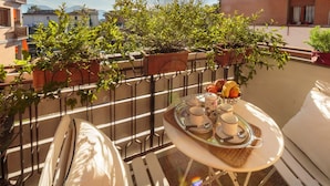 Varanda com mesa posta para refeição, rodeada por vasos de plantas e vista para edifícios.
