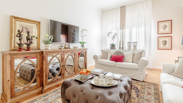 Sala de estar com sofá, banquinho e aparador com objetos decorativos.