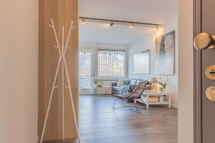 Uma sala de estar moderna com piso de madeira, uma poltrona de couro marrom, um sofá branco e uma mesa de jantar com abajur.