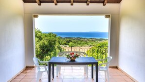 Uma varanda com mesa e cadeiras, oferecendo uma vista panorâmica do mar e vegetação.
