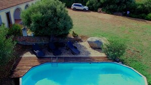 Uma piscina octogonal com deck de madeira, cercada por um muro de pedra e uma árvore.
