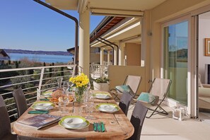 Mesa de jantar montada numa varanda com vista para o mar, cadeiras de exterior e uma porta de vidro que dá para um quarto.