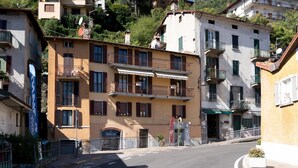 Um edifício de vários andares com varandas, uma loja com a placa "Bazar" e uma rua ampla em frente.