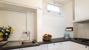 Cozinha com armários brancos, bancada preta, pia de aço inoxidável, chaleira azul e um cesto de flores.