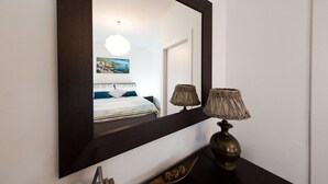 Quarto com um espelho grande, cama com roupa de cama listrada, abajur e uma pequena bandeja de madeira com objetos decorativos.