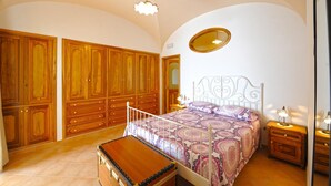 Quarto com cama, guarda-roupa de madeira e uma pequena mesa com abajur.