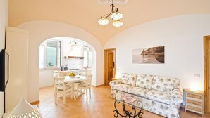 Uma sala de estar com sofá, mesa de jantar e cadeiras, e uma área de cozinha com janela.