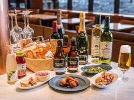 Uma mesa com diversas garrafas de cerveja, vinho e um copo de vinho branco, acompanhadas de pratos de comida.