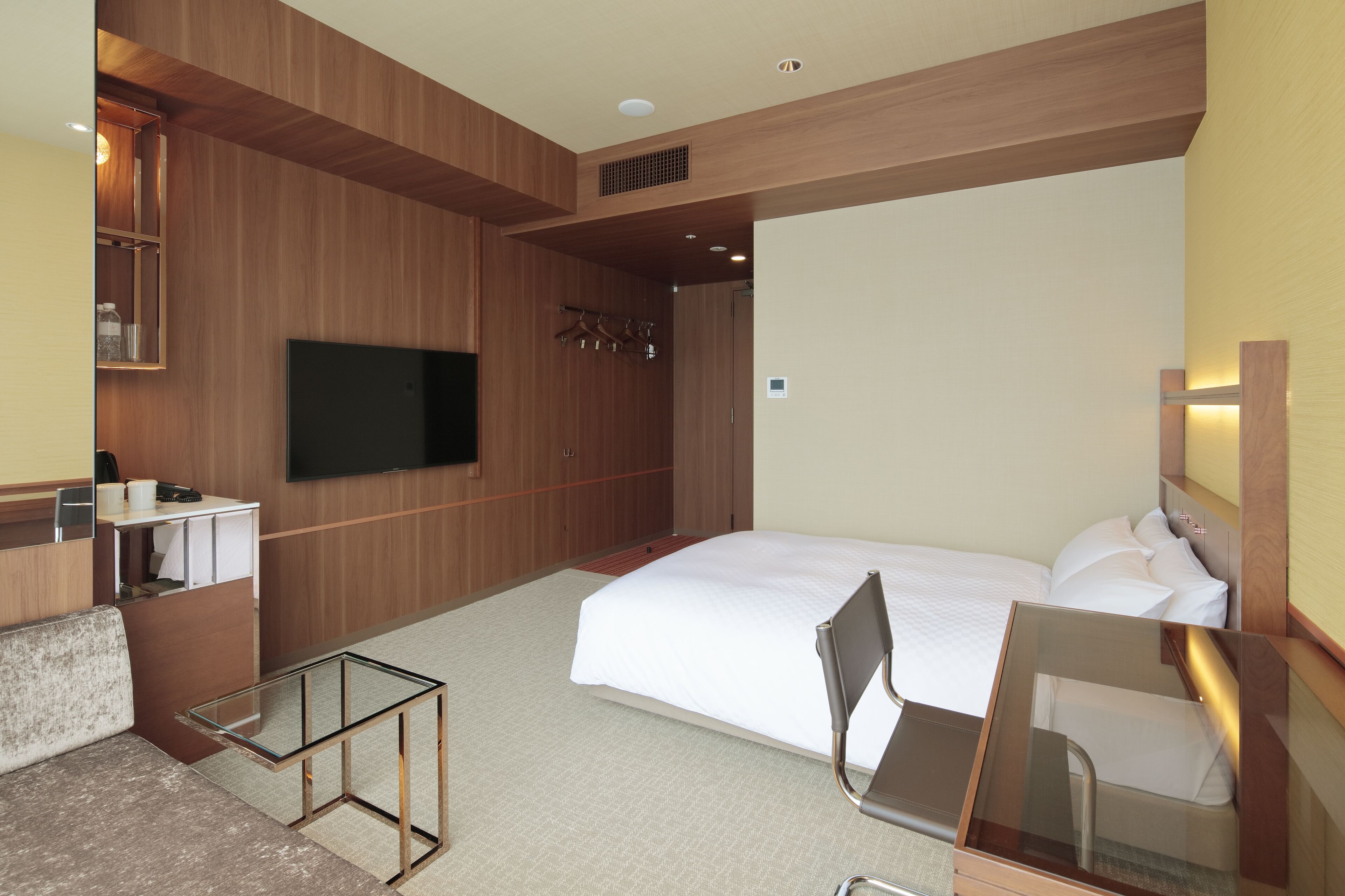 Quarto de hotel com cama, televisão, escrivaninha e área de estar.