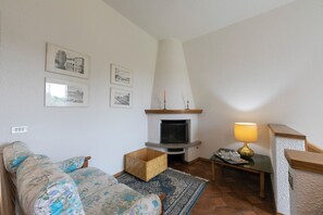 Uma sala de estar com sofá, lareira, abajur e quadros nas paredes.