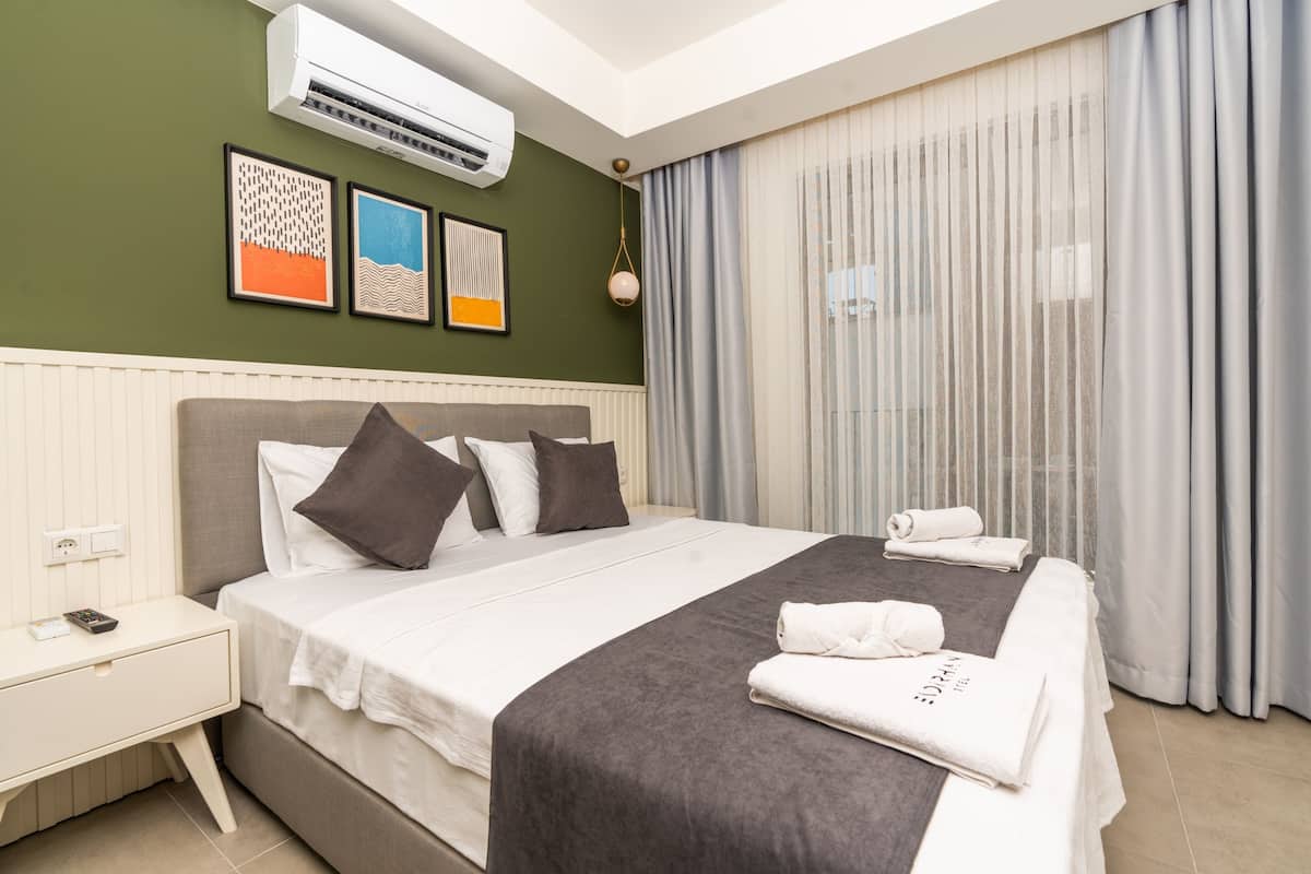 Quarto de hotel com uma cama grande, mesa de cabeceira, ar condicionado e janela com cortinas.