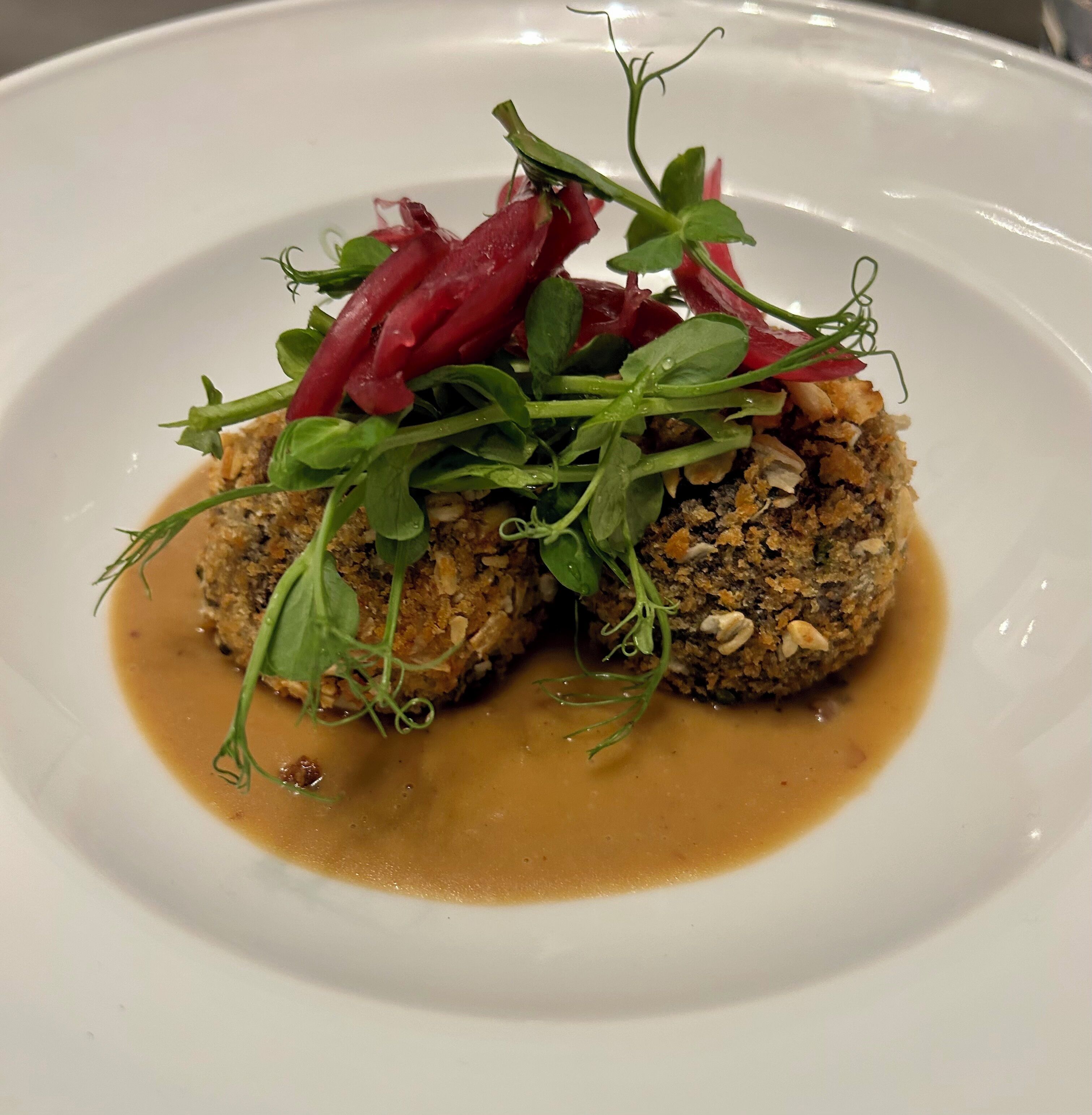 Um prato com duas porções de comida, decorado com folhas e vegetais vermelhos, e um molho castanho.