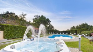 Uma banheira de hidromassagem com painel de controle, piscina e cadeiras de descanso num jardim.