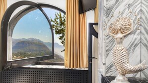 Quarto com uma grande janela que oferece vista para as montanhas, uma escultura decorativa de sereia e uma parede de mármore.