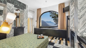 Quarto de hotel com cama, janela com vista para montanhas, televisão de tela plana e banheiro com parede de mármore.