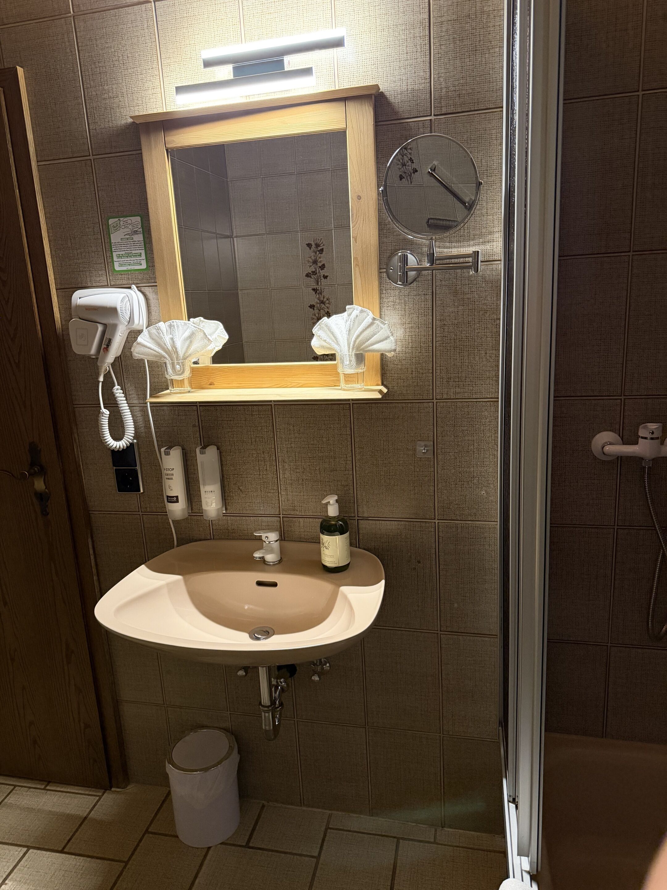 Casa de banho com lavatório, espelho, secador de cabelo e chuveiro.