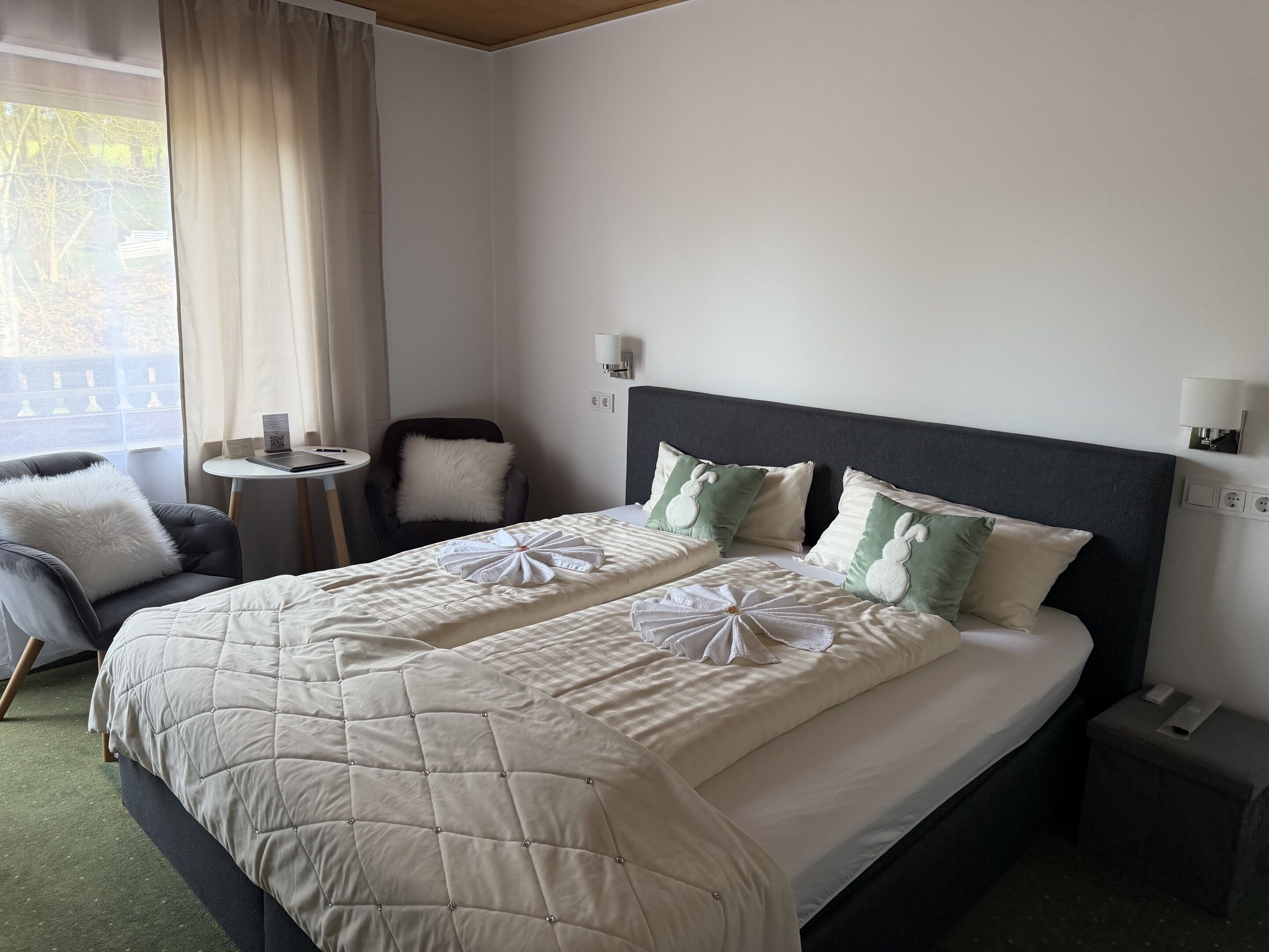 Quarto de hotel com uma cama grande, uma cadeira, uma mesinha e vista para o exterior.