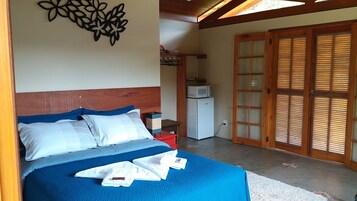 Quarto com cabeceira de madeira, cama com roupa de cama azul, decoração de parede branca, micro-ondas e porta de vidro deslizante.