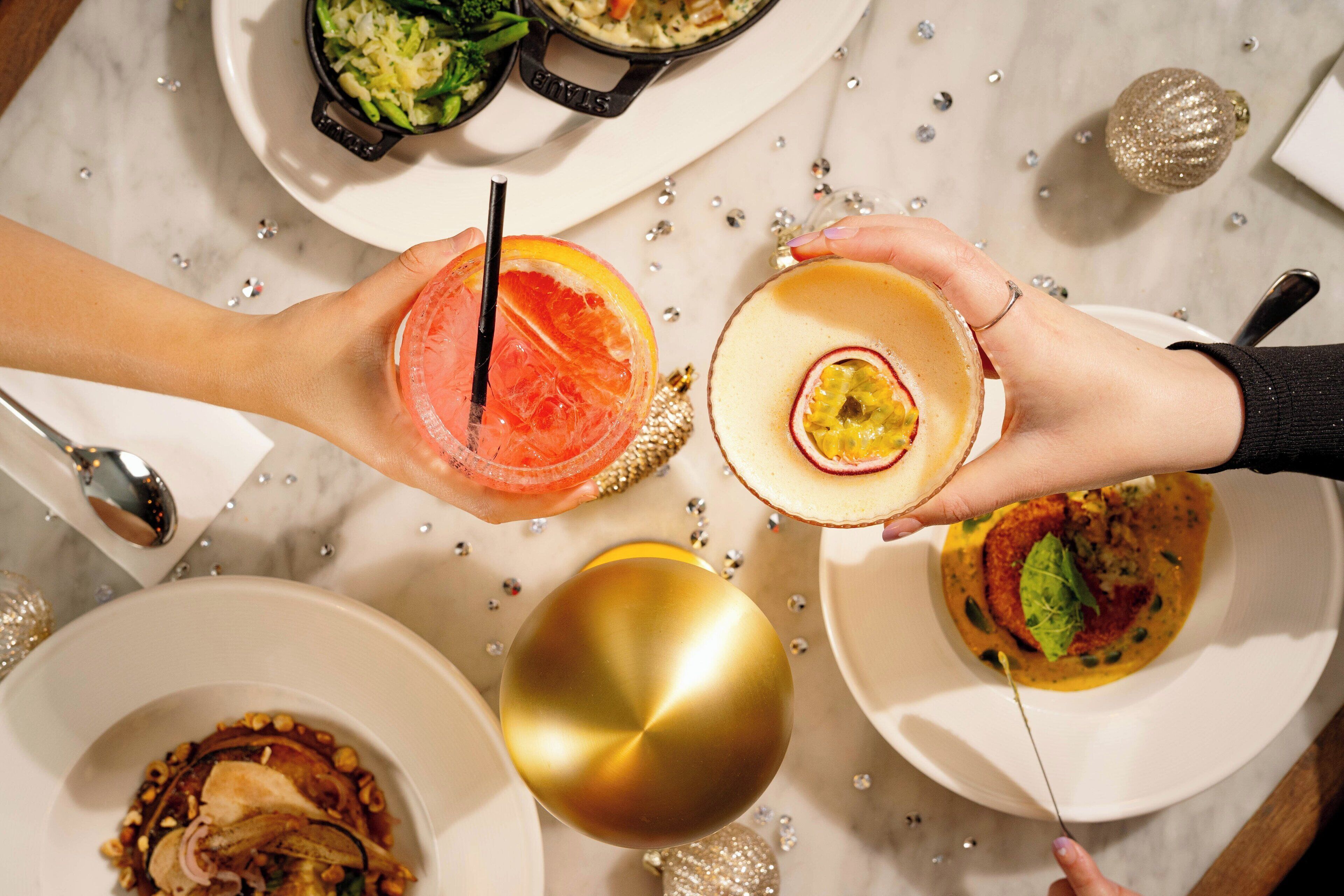 Uma mesa com diversos pratos e bebidas, incluindo uma bebida de toranja com canudo, um prato com uma fatia de fruta e uma tigela com molho.
