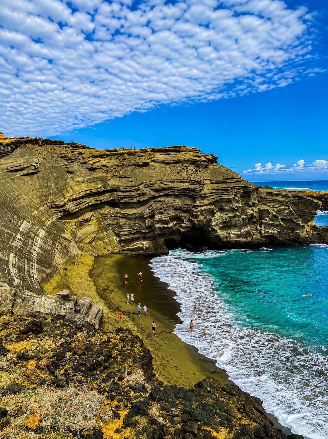 Paisagem costeira com formações rochosas sobrepostas, uma praia e águas azul-claras.
