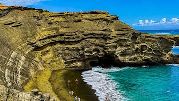 Paisagem costeira com formações rochosas sobrepostas, uma praia e águas azul-claras.