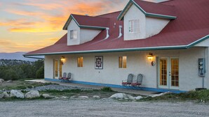 Uma casa de dois andares com telhado vermelho, varanda com cadeiras e vista para as montanhas.