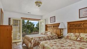 Quarto com duas camas, cabeceira de madeira, mesa de cabeceira com abajur e porta que dá para uma varanda.