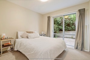Quarto com uma cama grande, mesa de cabeceira com abajur, e vista para o verde através de uma porta de vidro deslizante.