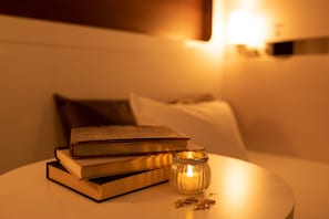 Uma mesa de cabeceira com livros, uma vela e um objeto decorativo pequeno.