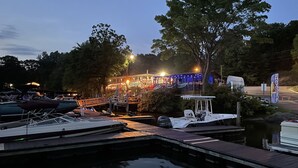 Um restaurante à beira-mar com mesas ao ar livre, barcos atracados e um pequeno cais.