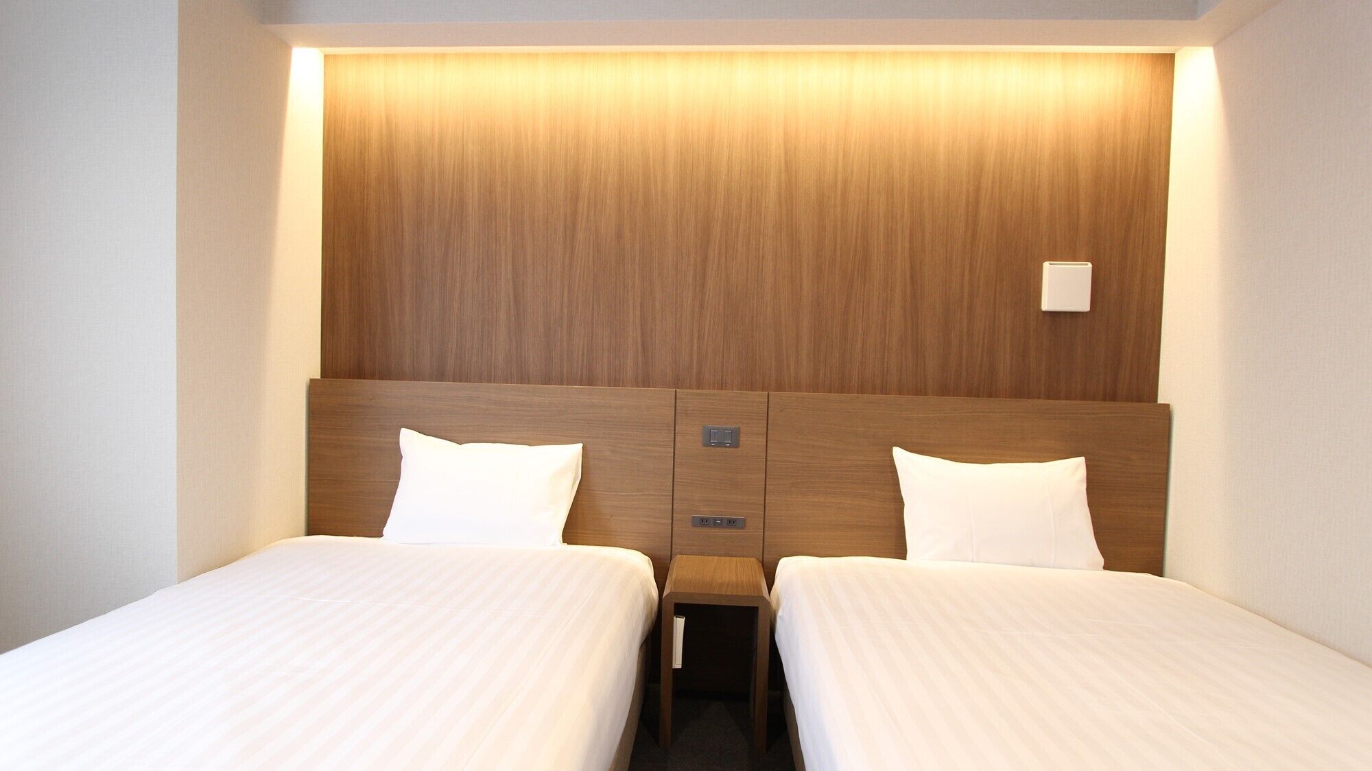Quarto de hotel com duas camas, cabeceira de madeira e mesa de cabeceira.