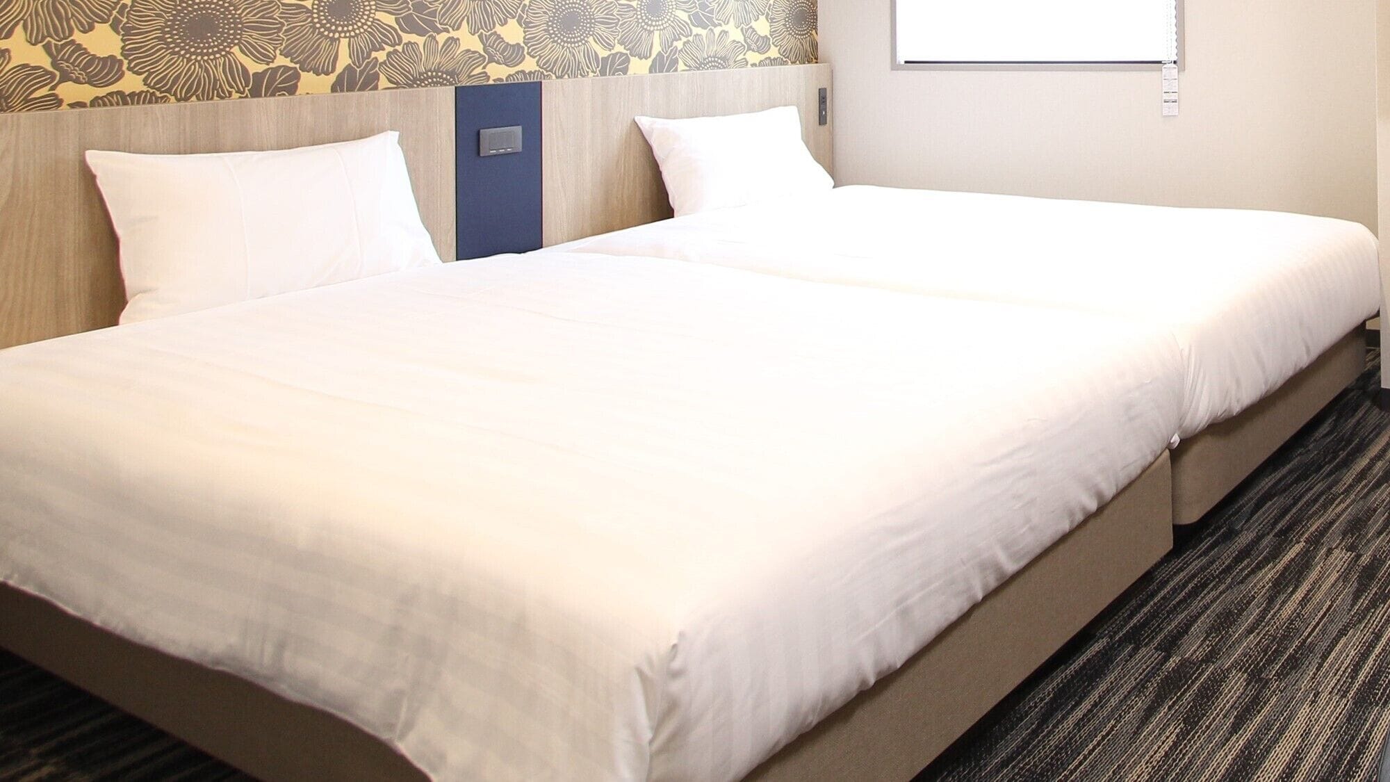 Quarto de hotel com uma cama grande, painel de controle na cabeceira e papel de parede estampado.