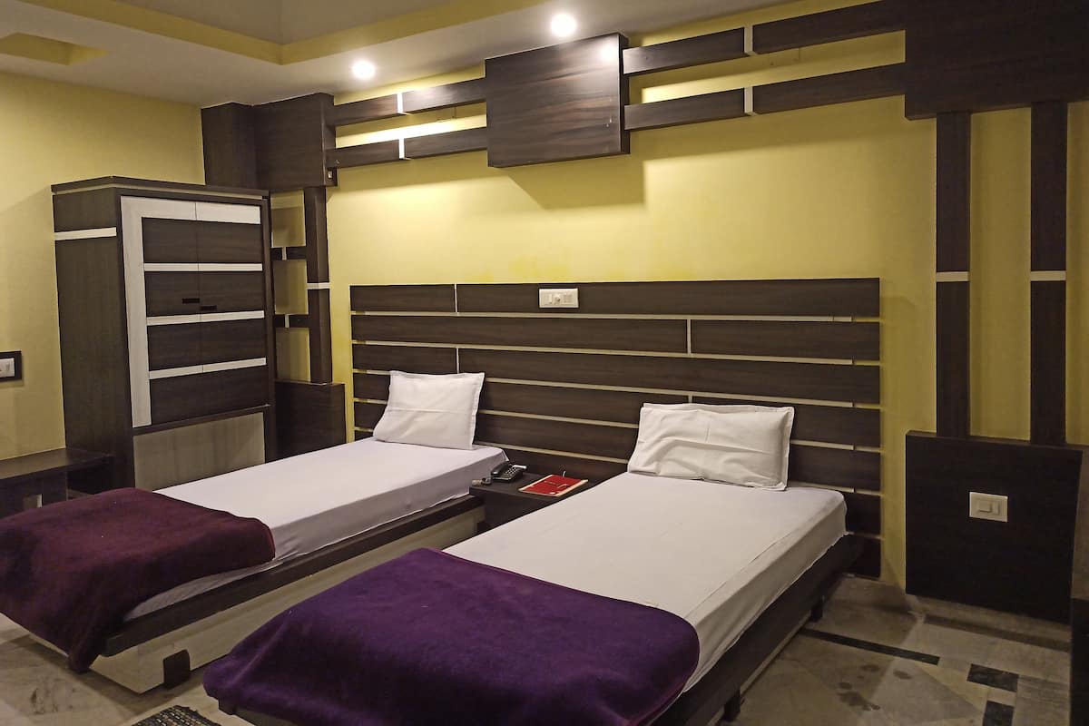 Quarto de hotel com duas camas de solteiro, um guarda-roupa e uma televisão presa à parede.
